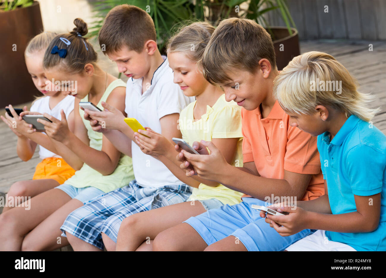 Group of friendly kids playing with mobile phones together outdoors ...