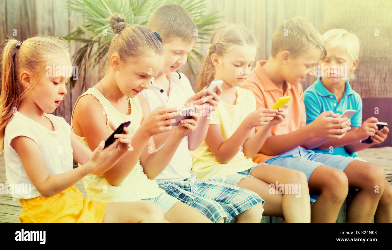 Group of happy children playing with mobile phones together outdoors ...