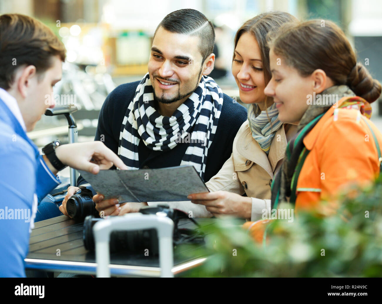 Group of young tourists checking direction in map at street cafe ...