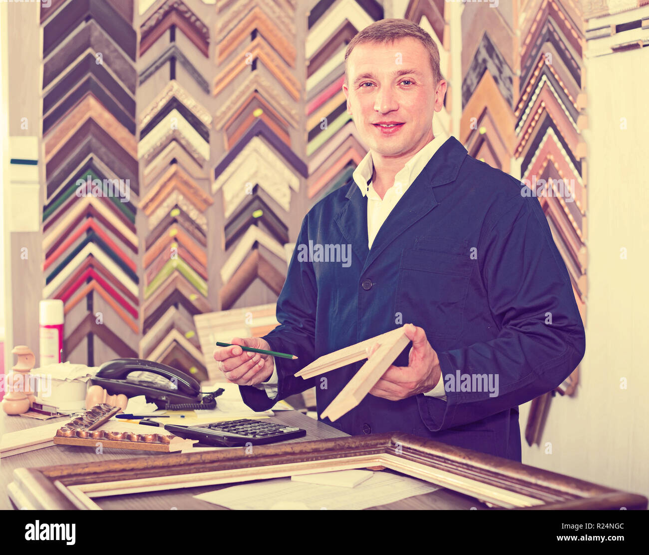 positive man seller standing in picture framing studio with wooden ...