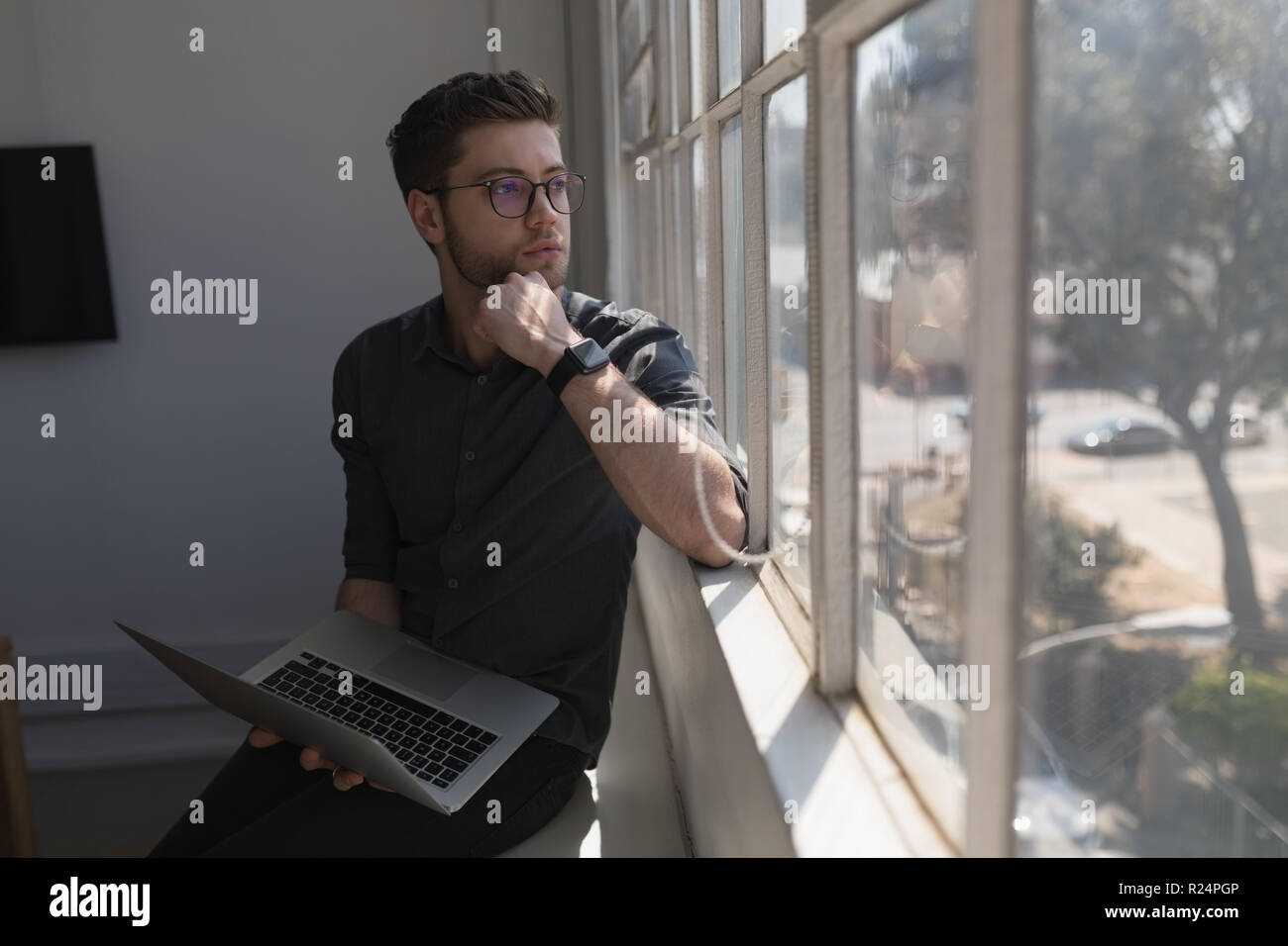 Executive looking through window while using laptop in office Stock ...