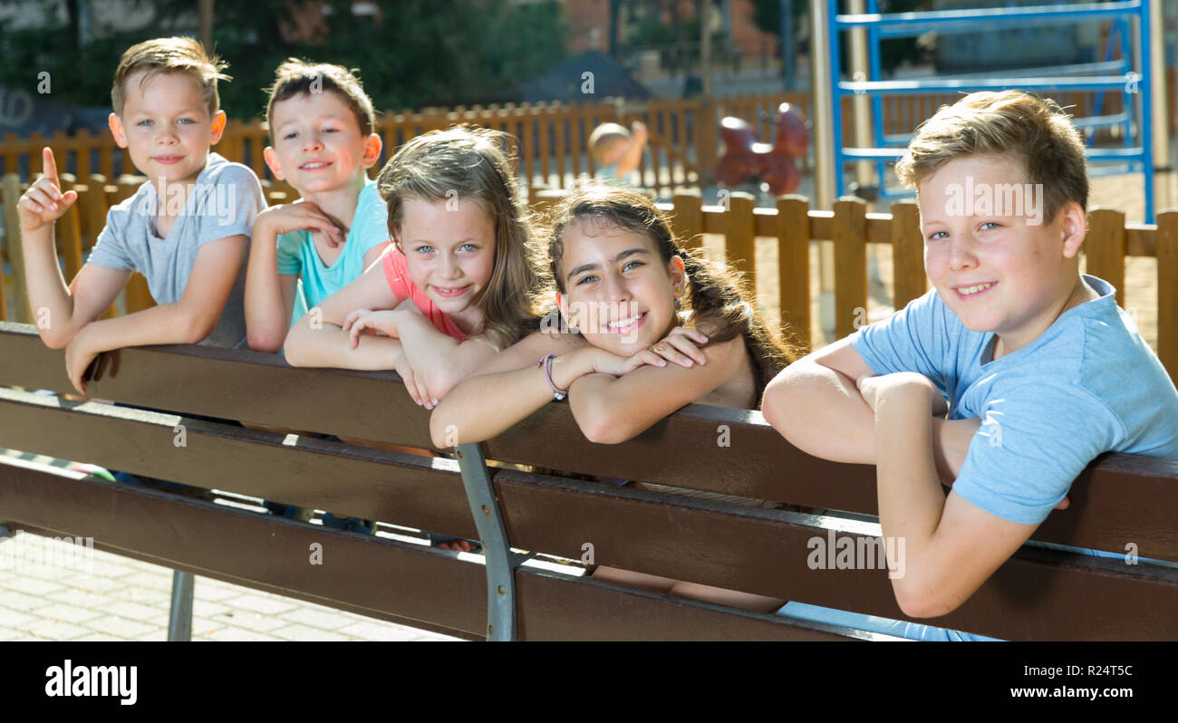 Five children sitting on a bench at the playground and point to ...