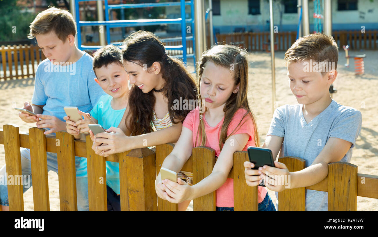 Five glad children sitting and playing in smartphone at the playground ...