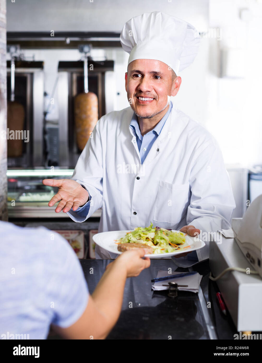 smiling man chef in uniform giving order with kebab plate to customer ...