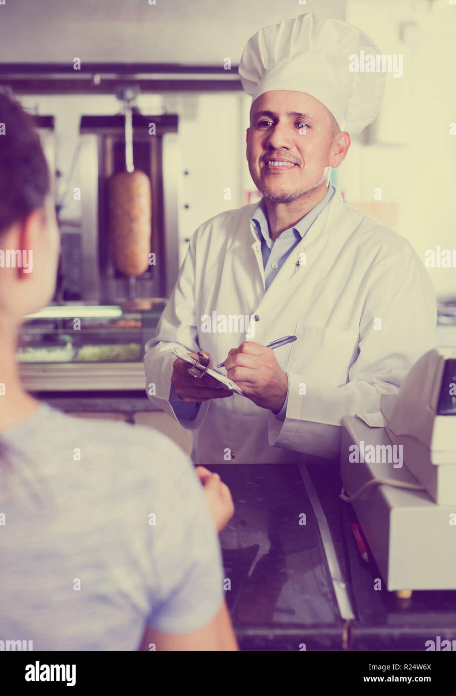 cheerful european mature man cook taking order from customer on counter ...