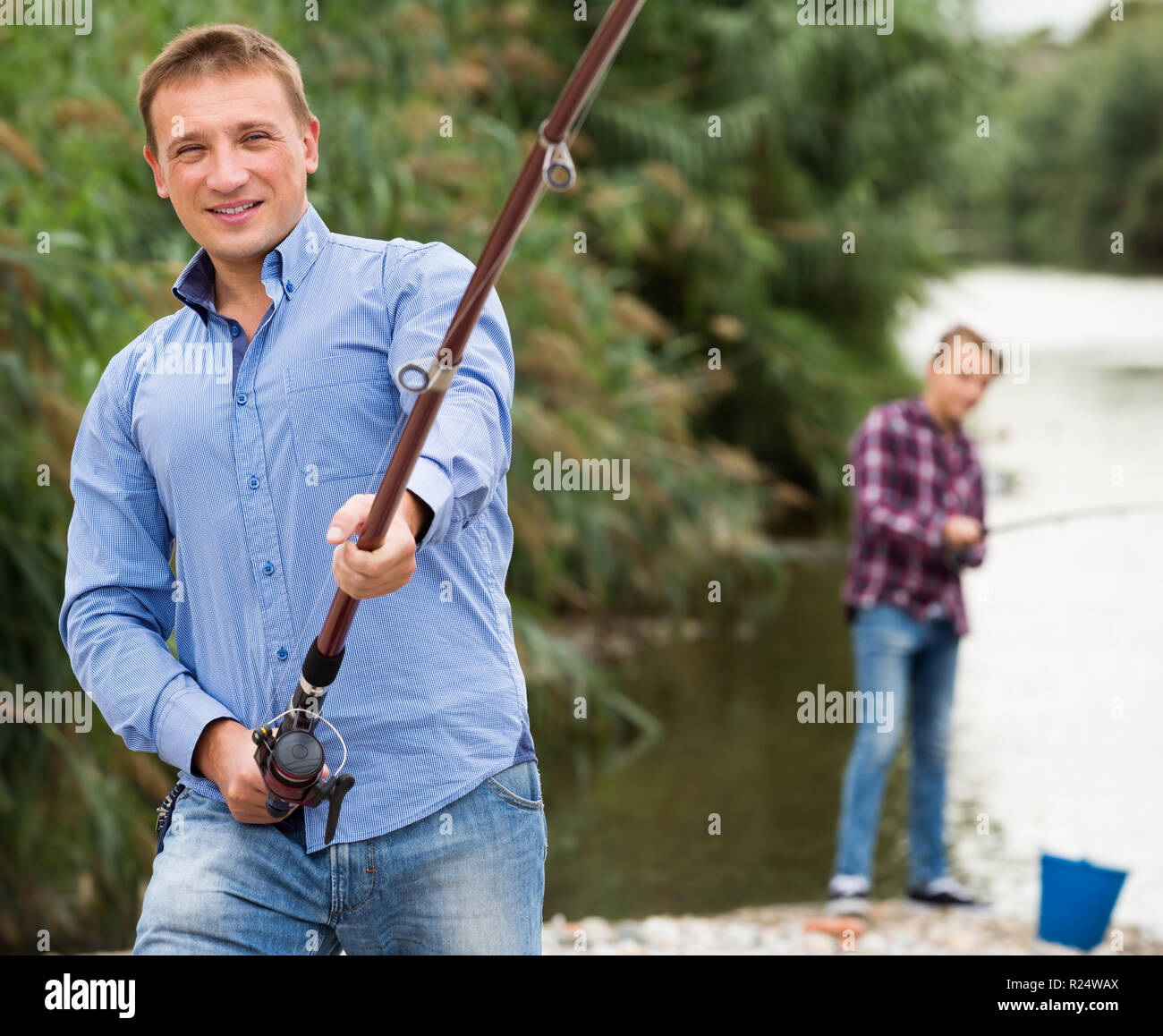 Positive adult man fishing using rod from the water side on lake Stock ...