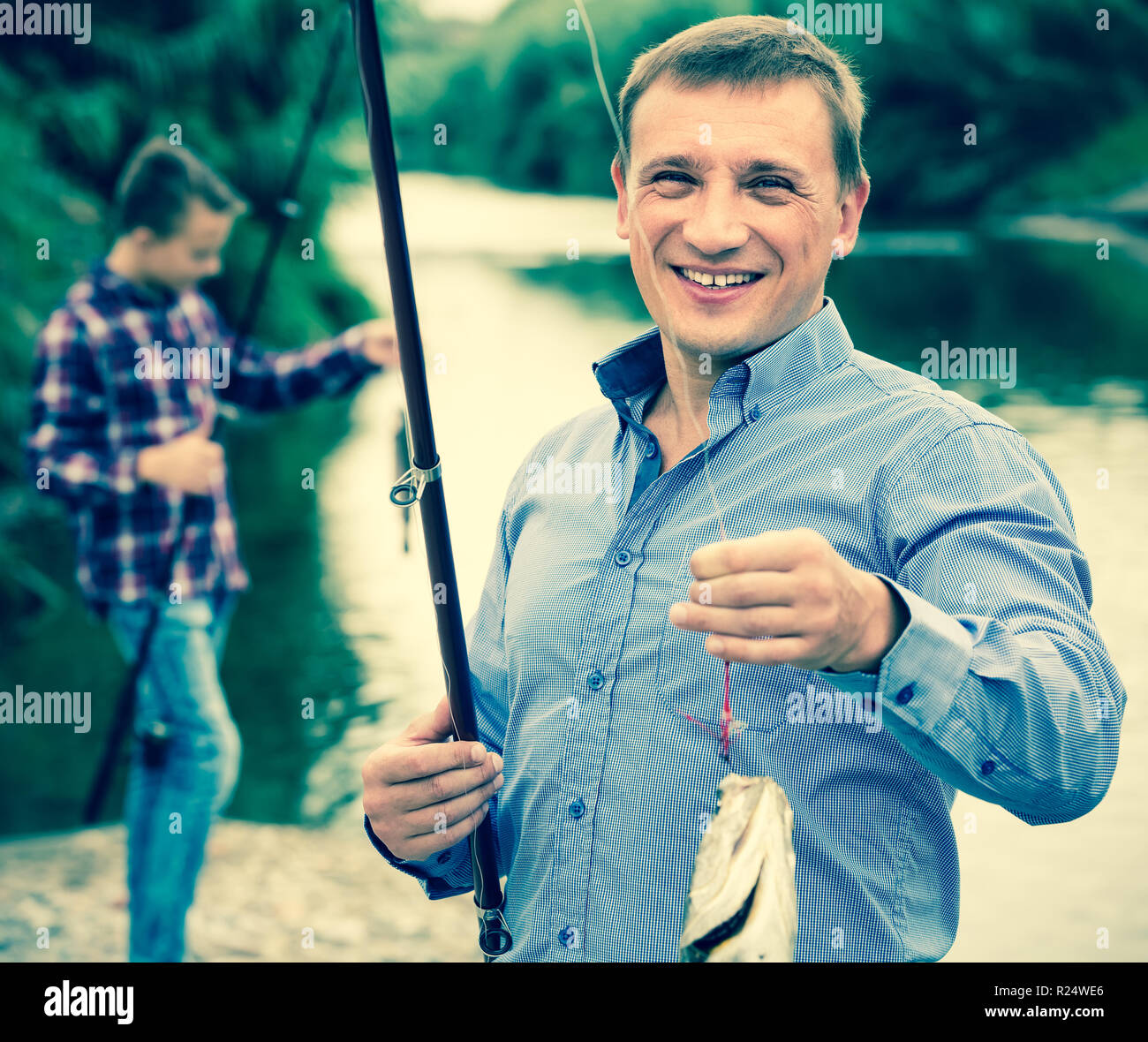 portrait of cheerful man showing fresh catch fish on lake shore Stock ...