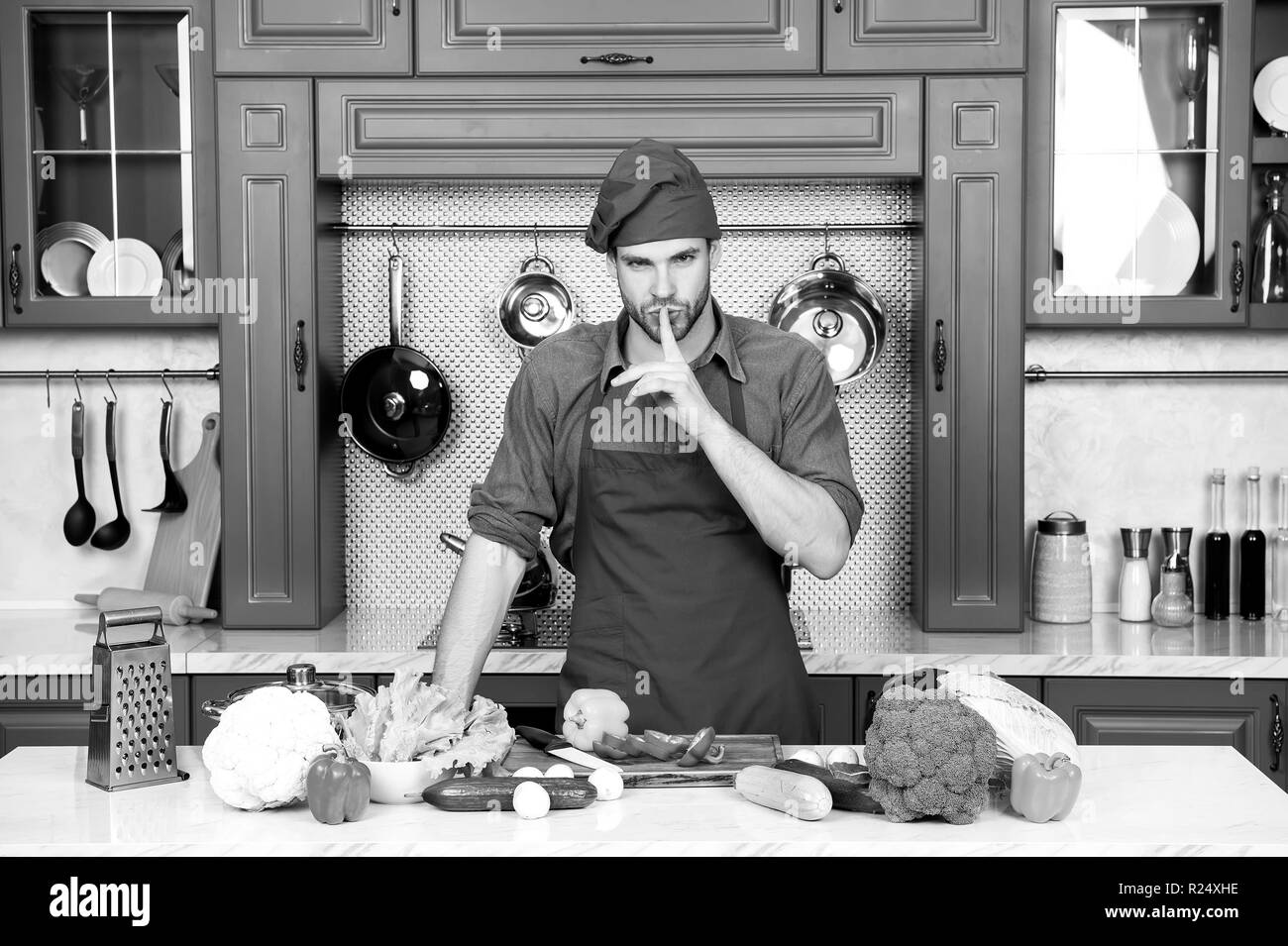 Chef with silence gesture finger at table with vegetables. Man cook ...