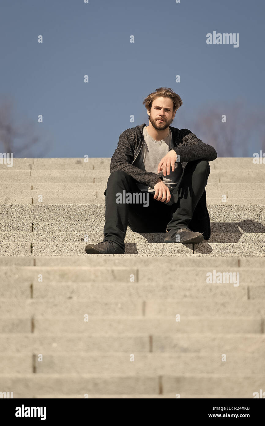thoughtful young man sitting on a flight of steps staring into the ...