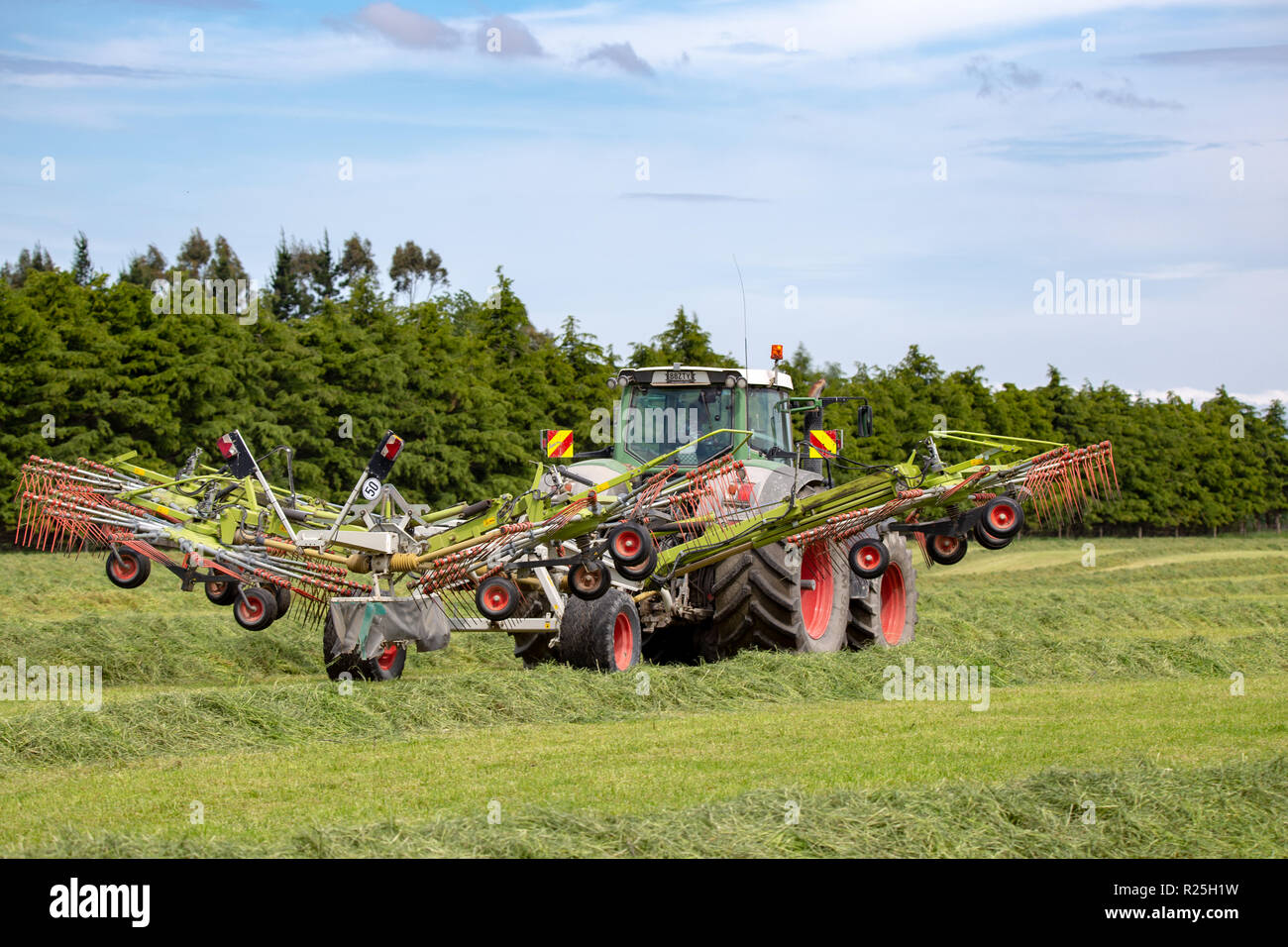 A Fendt tractor and tedder work in a farm field raking cut grass into ...