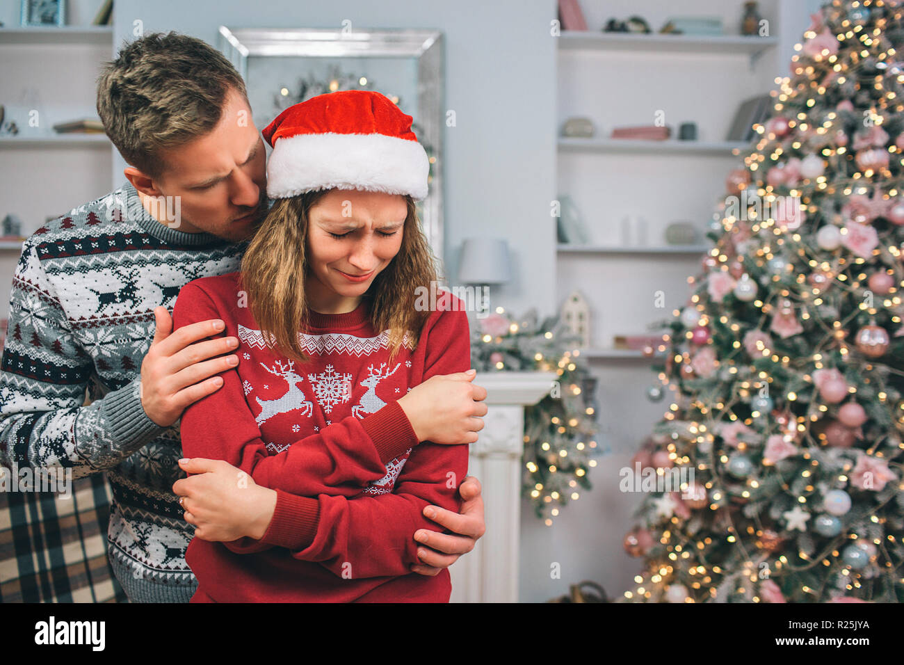 Careful young man trying to calm dowb woman. He stands behind her in decorated room. She ...