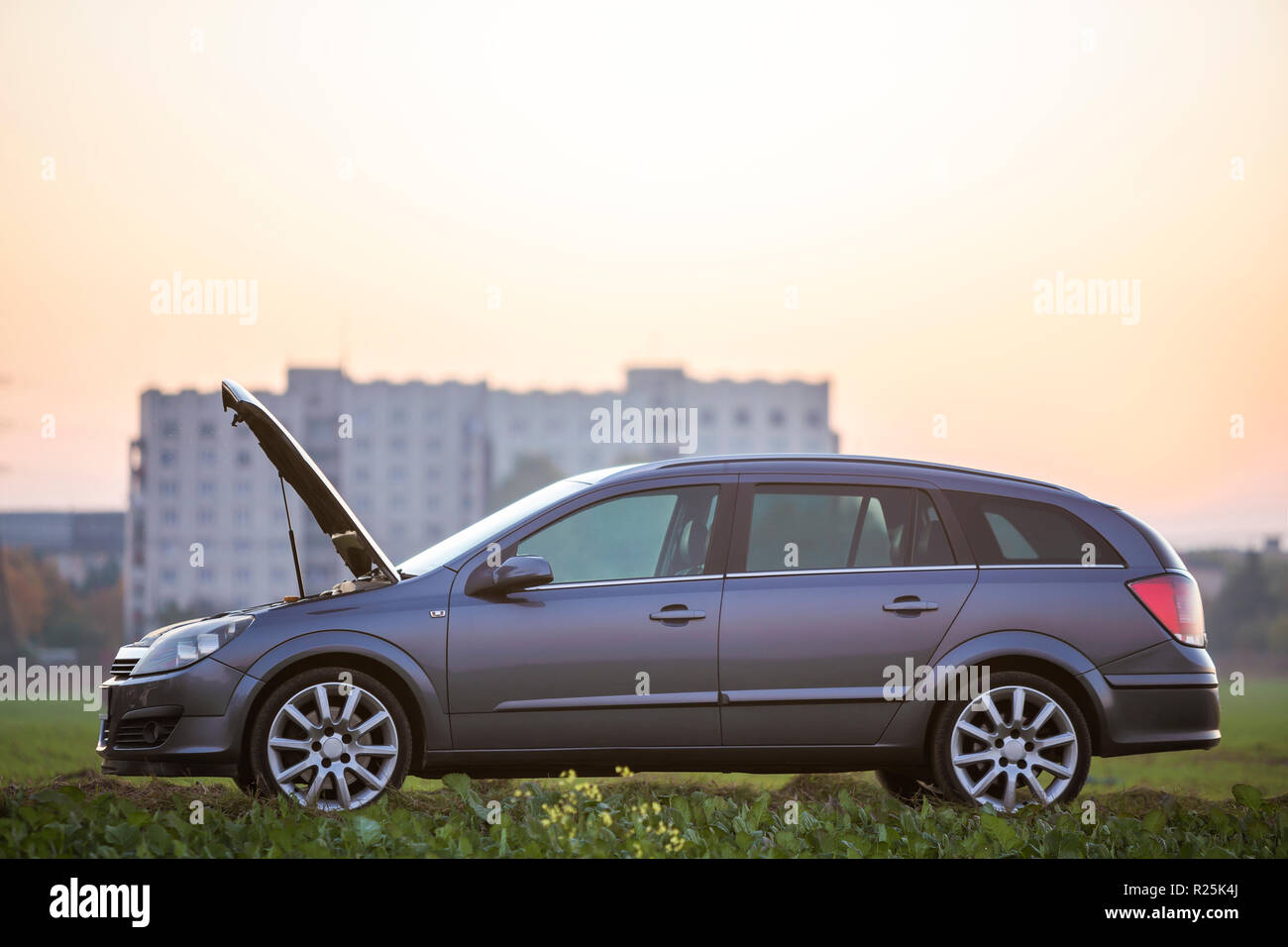 Side view of empty silver car with open hood on empty gravel field road ...