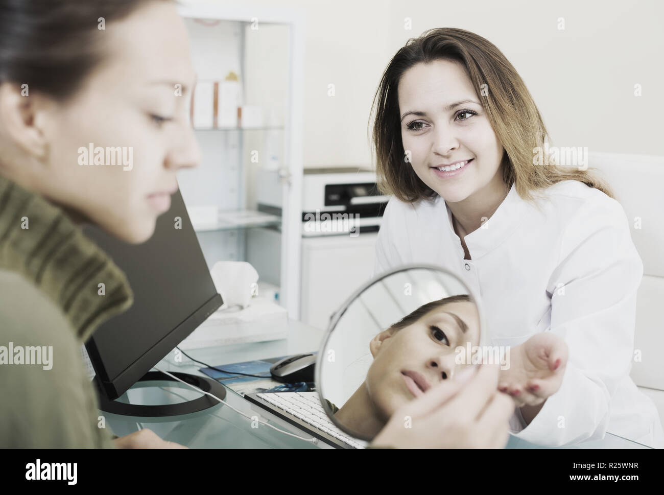 Young smiling woman looking at mirror during consultation with doctor ...