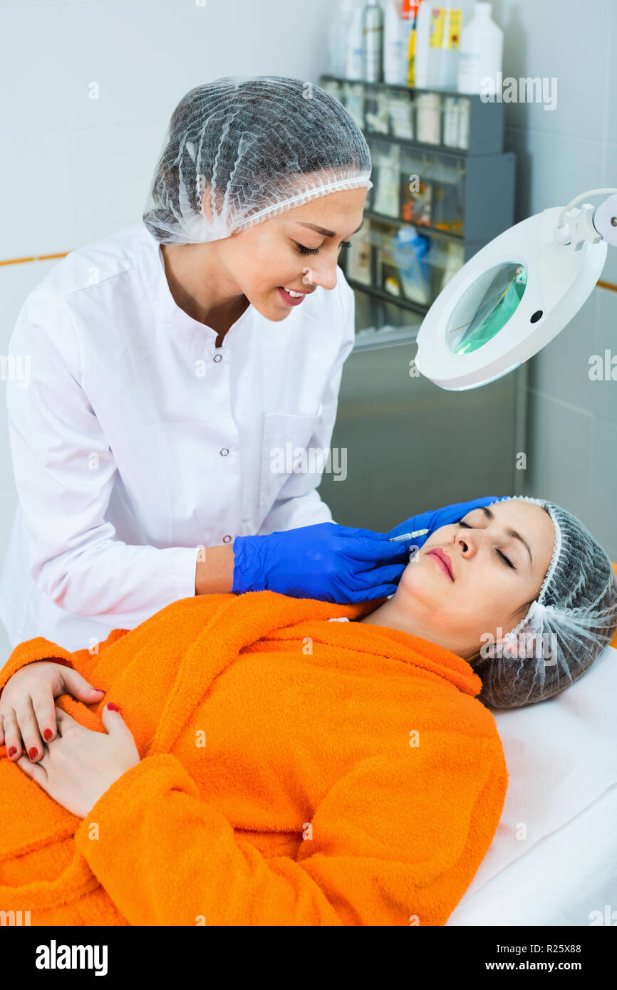 Positive smiling female doctor doing beauty injection to young woman ...
