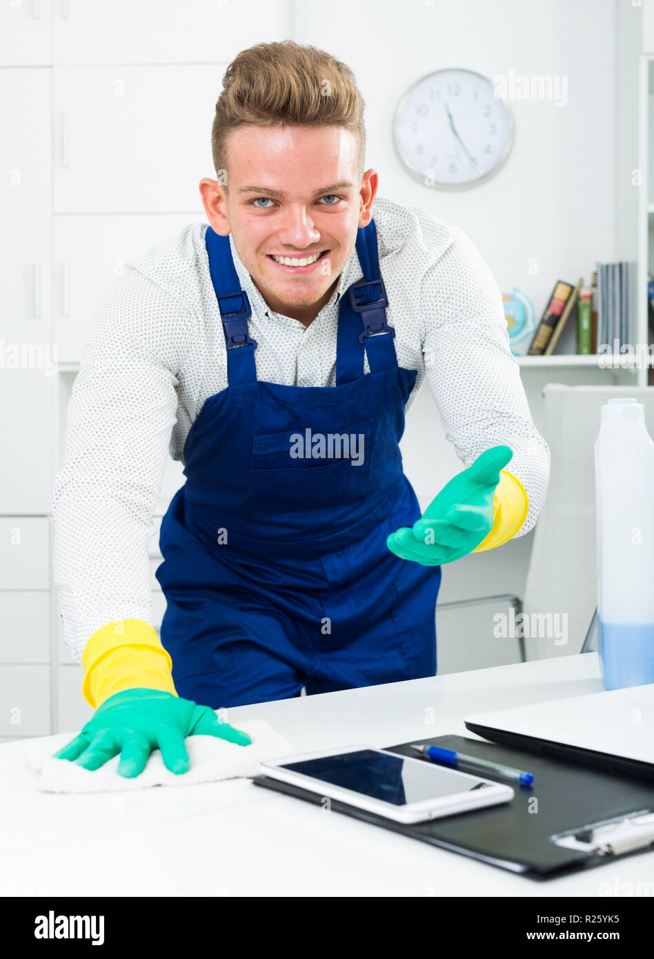Young male janitor dusting office desk and smiling indoors Stock Photo ...