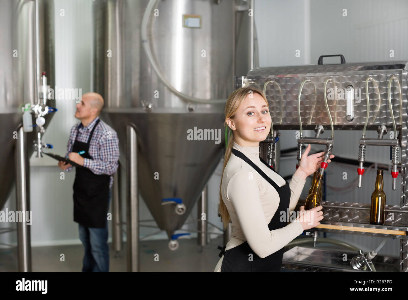 Young cheerful woman wearing uniform using the bottling equipment on ...