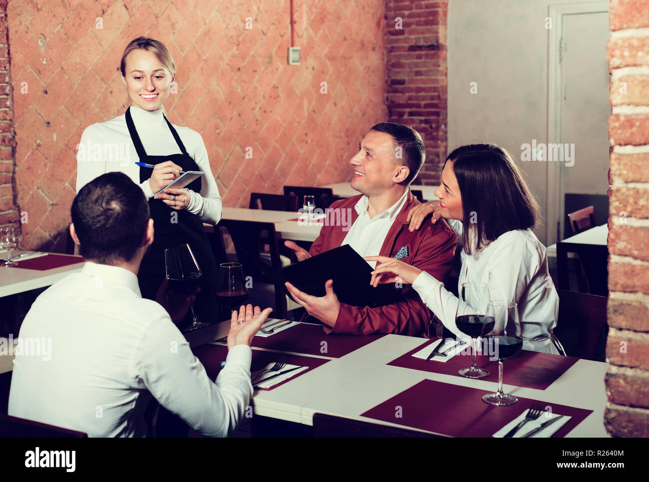 Young smiling female waiter taking order from visitors in country ...
