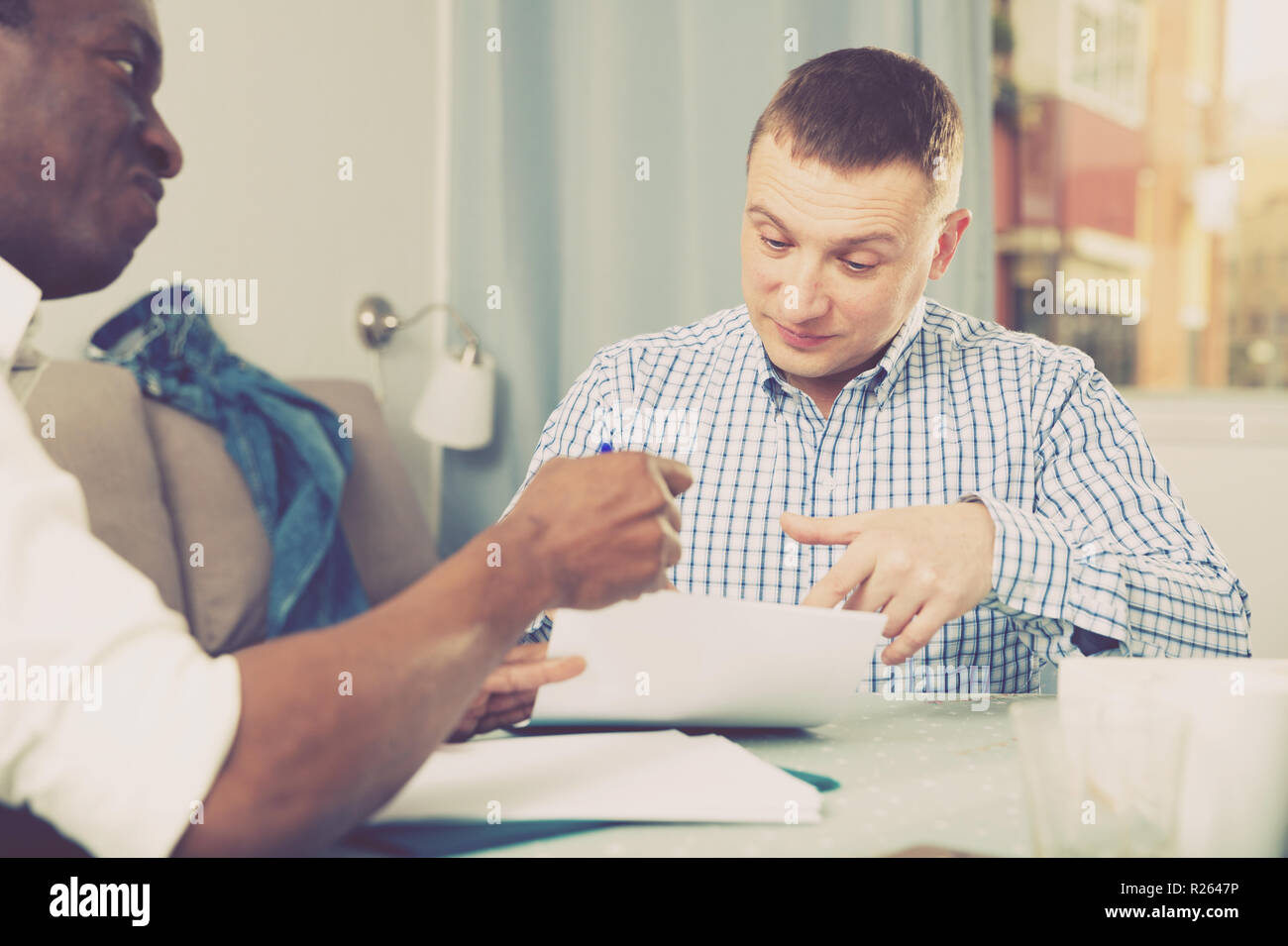 Portrait of two men in serious discussion at home table while analysing ...