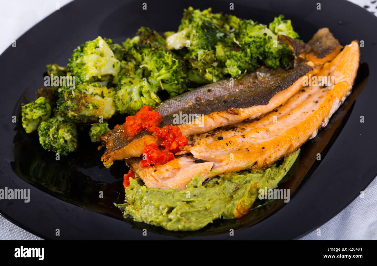 Fried river trout fillet with broccoli and various sauces on black ...