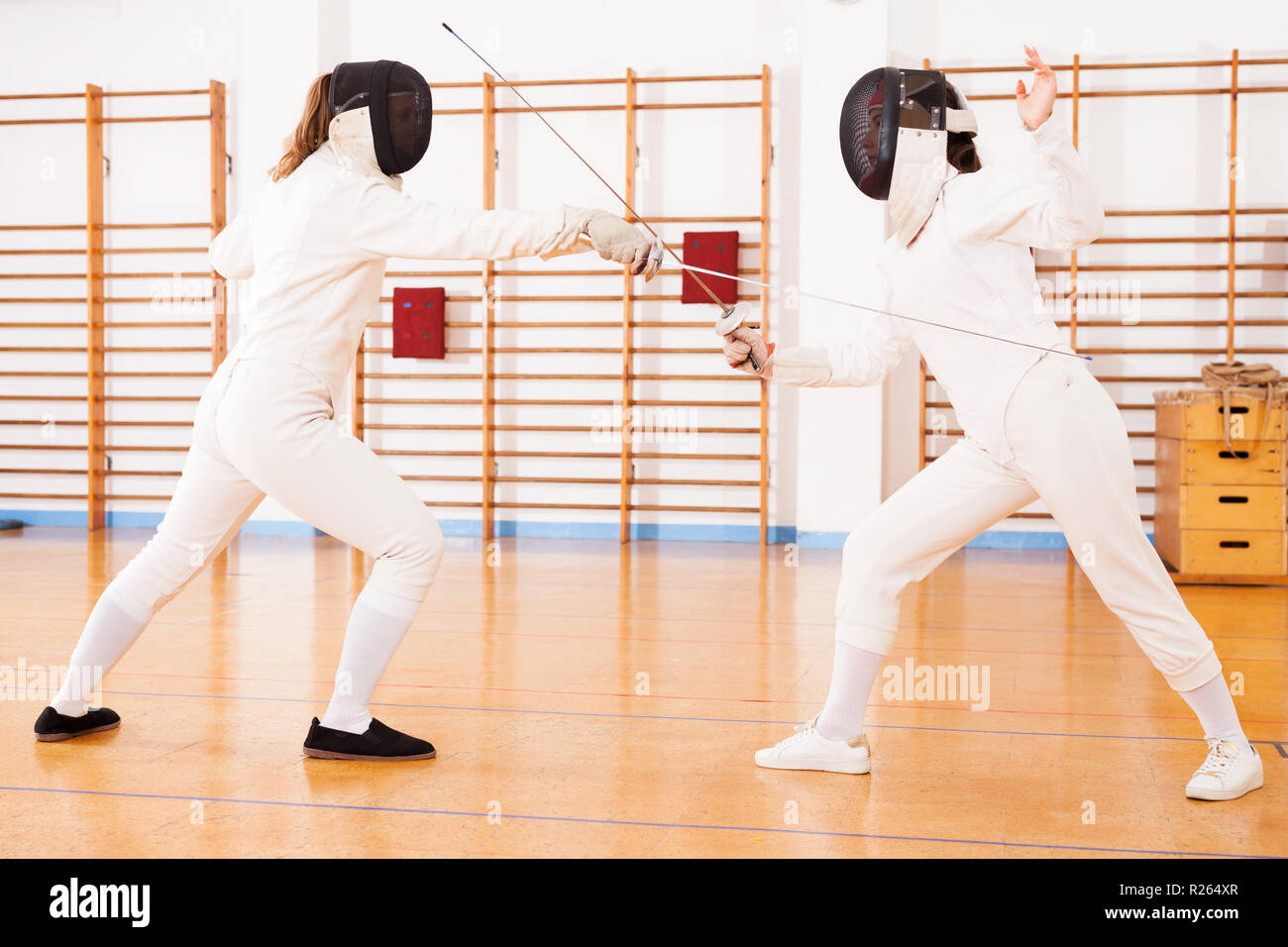 young female athletes in uniform practicing movements at fencing battle ...