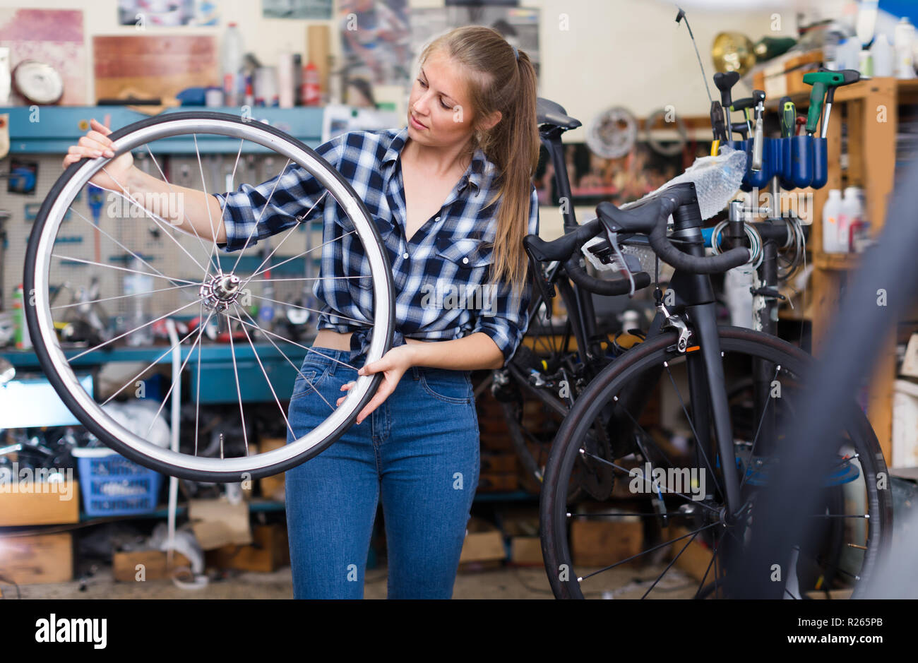 Portrait of nice female who is repairing wheels of bicycle in workshop ...