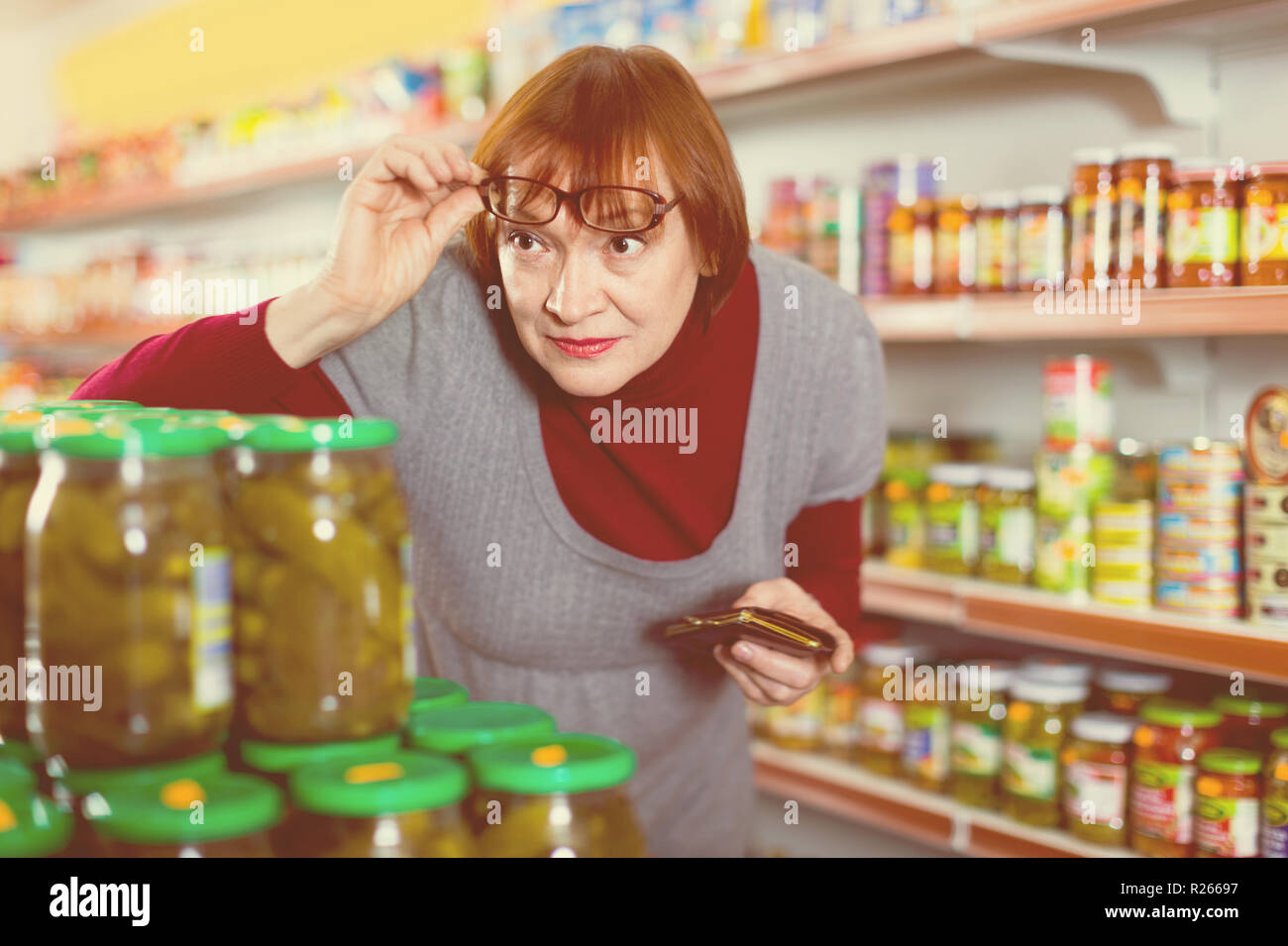 Adult smiling female customer holding glass jar of cucumbers in the ...
