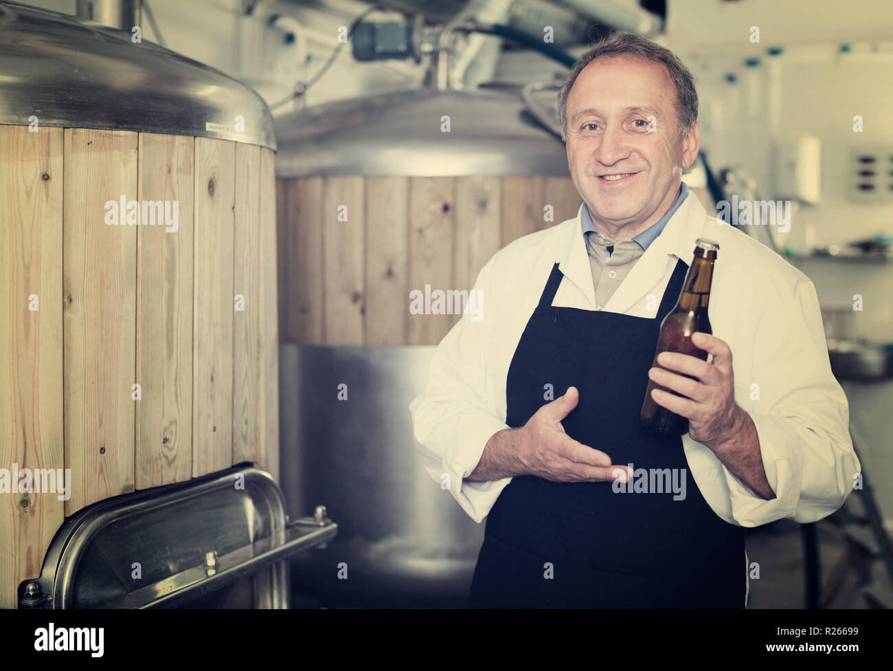 Portrait of brewer who is standing with bottle for beer on his ...