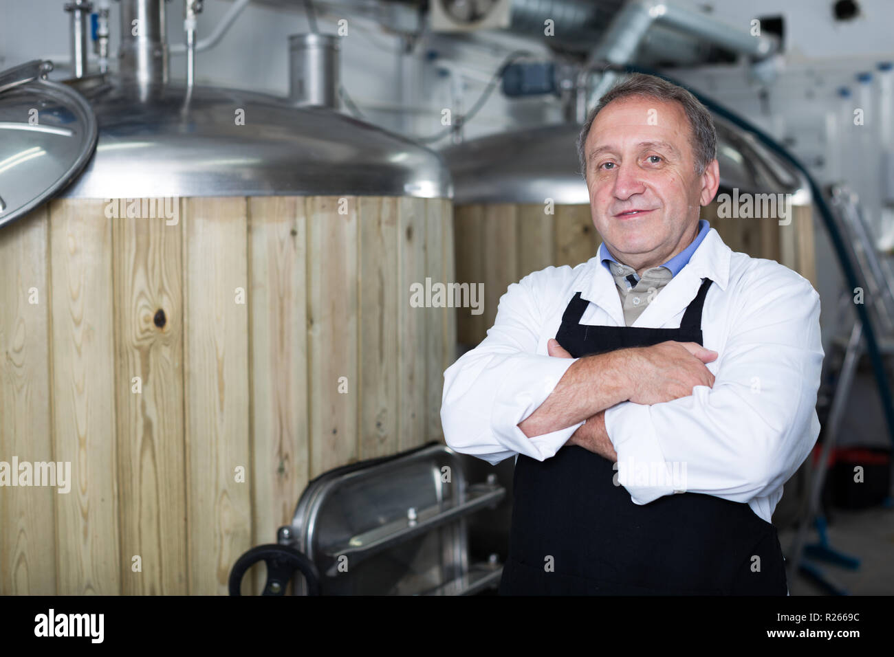 Brewer is standing near reservoir for beer on his workplace indoor ...