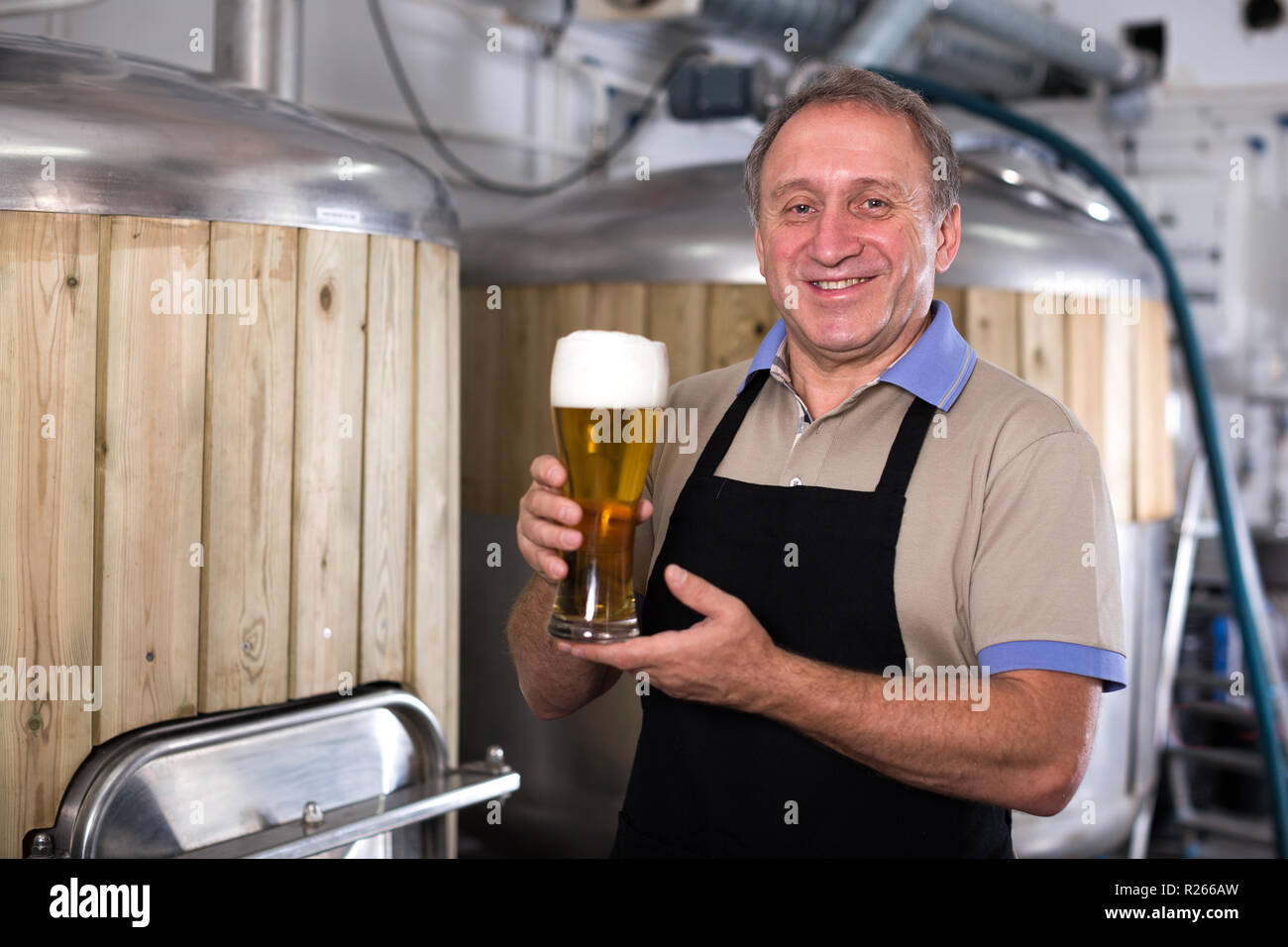 Brewer is standing with beer with foam in glass on his workplace indoor ...