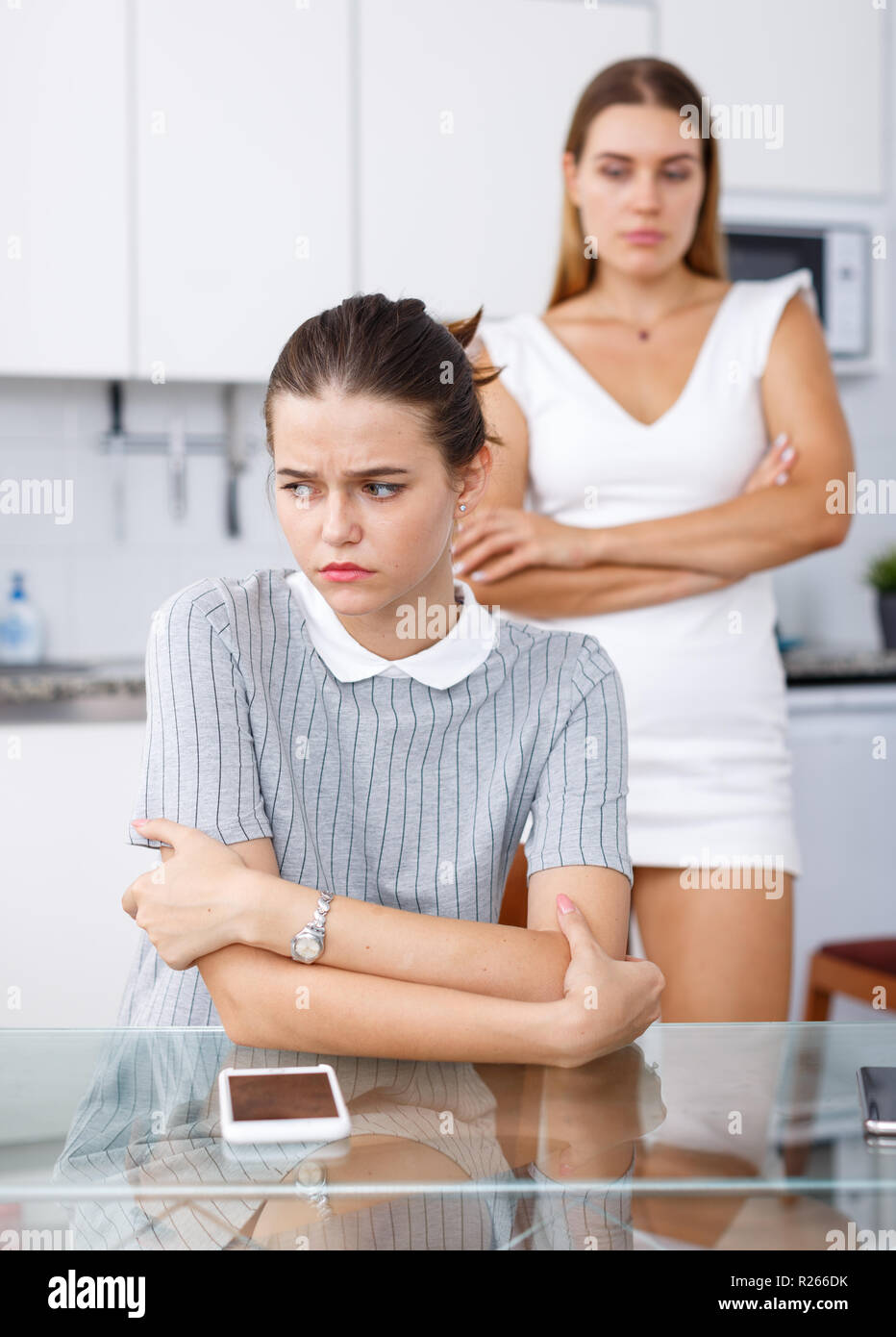 Sad girl sitting at table after conflict, woman friend on backround ...