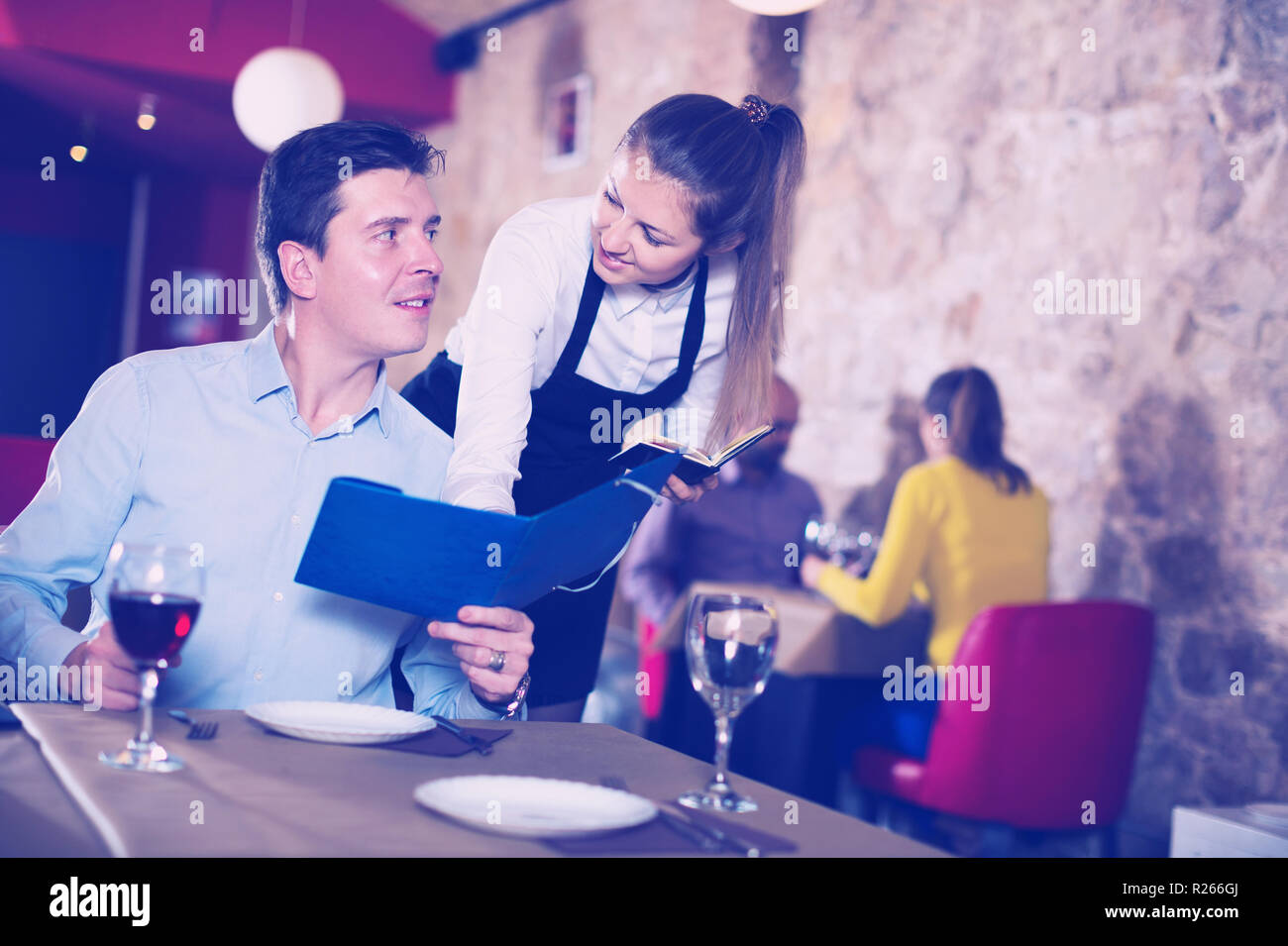 Young smiling waitress taking order from young man in restaurant ...