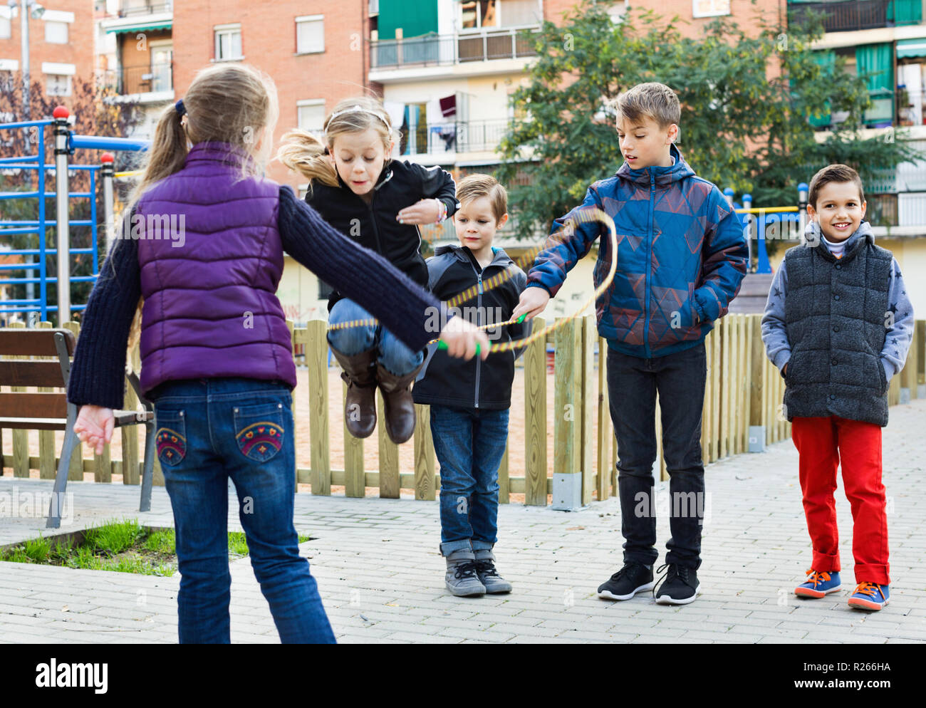 Positive smiling cheerful kids playing in jump rope game at city street ...