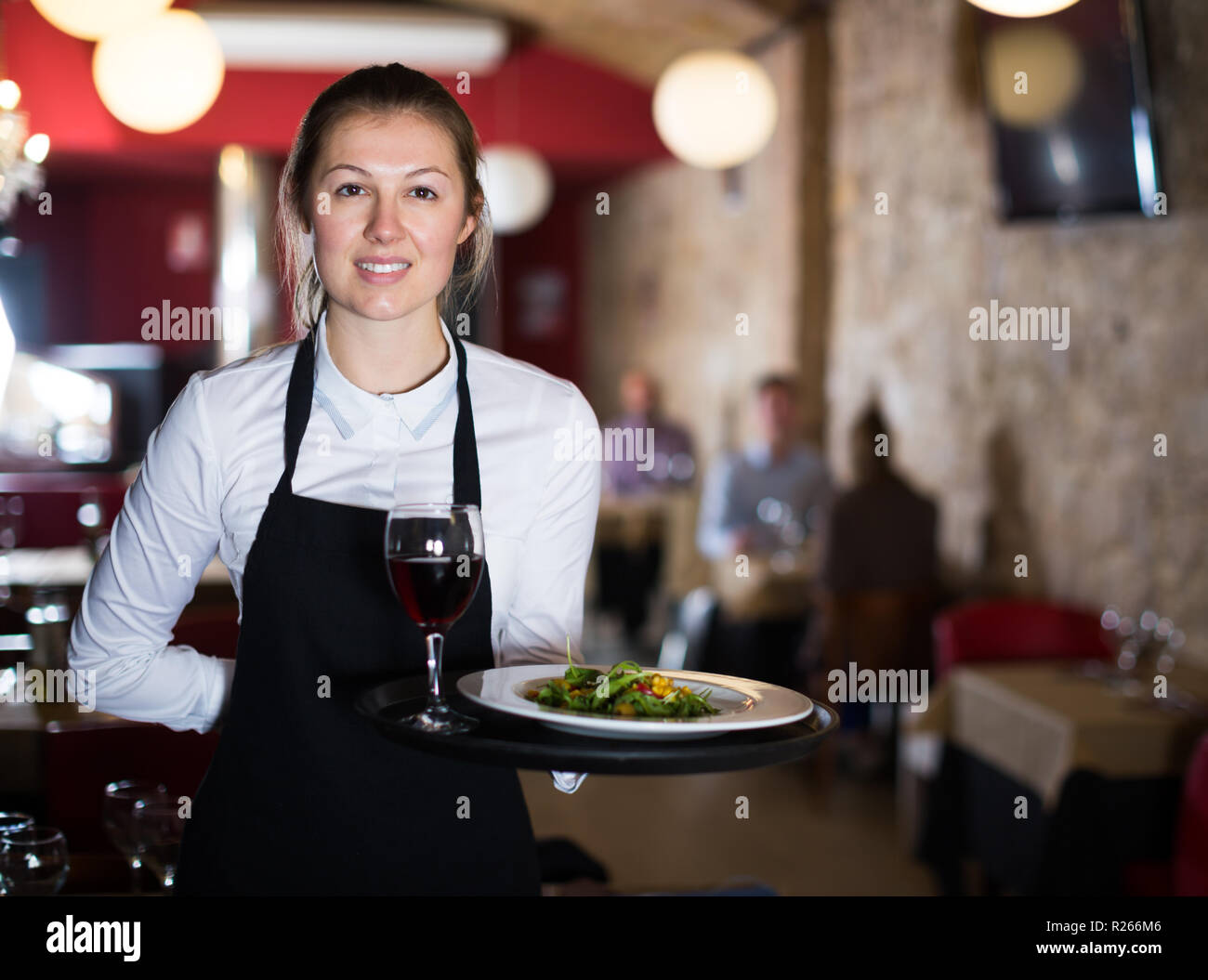 Smiling young woman waitress with serving tray welcoming in restaurant ...