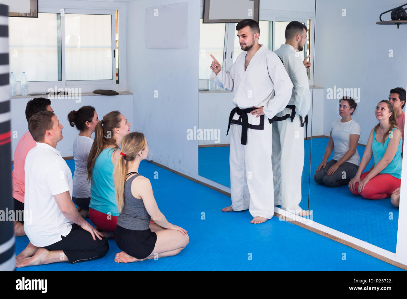 Beardy young coach is showing new martial moves to adults in karate ...