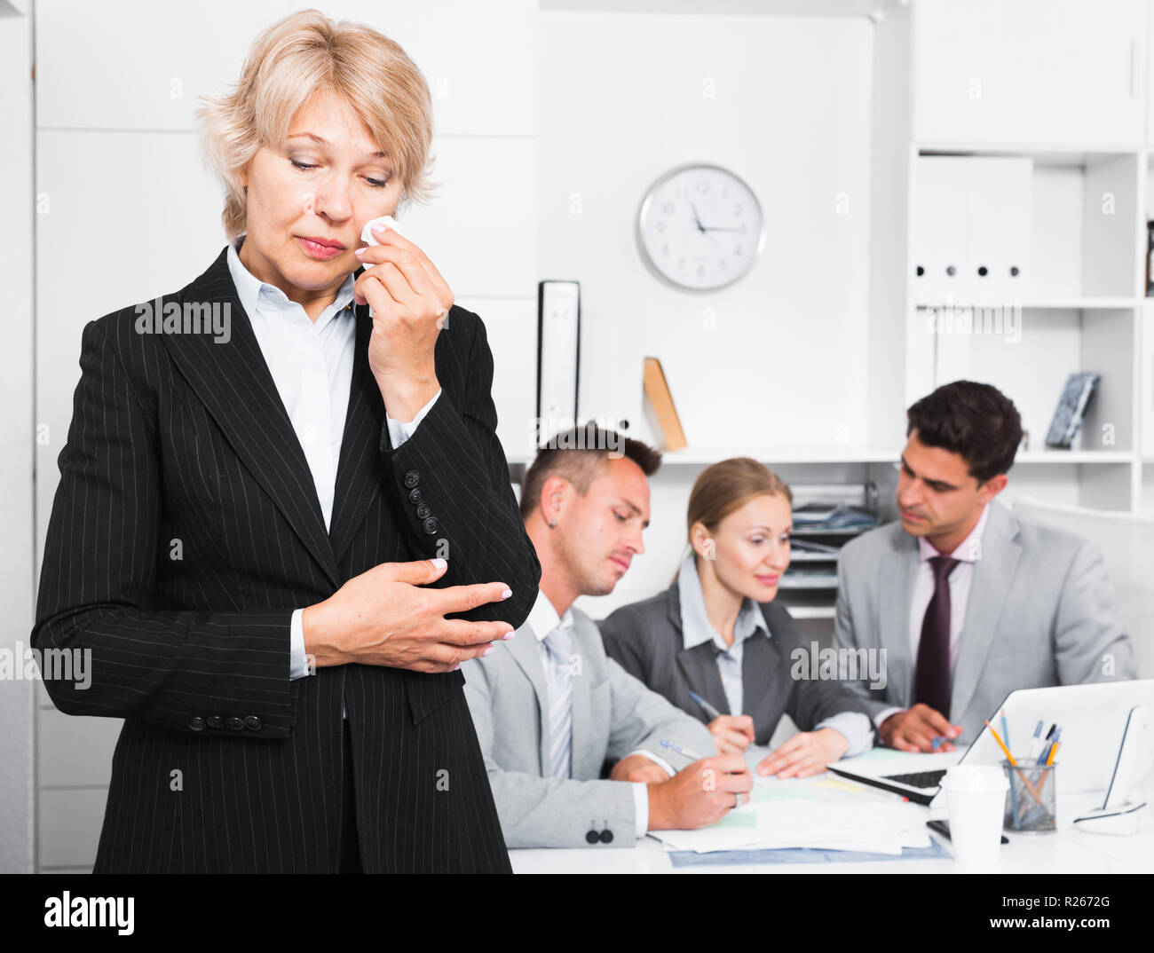 Business woman crying standing in office with working colleagues behind ...