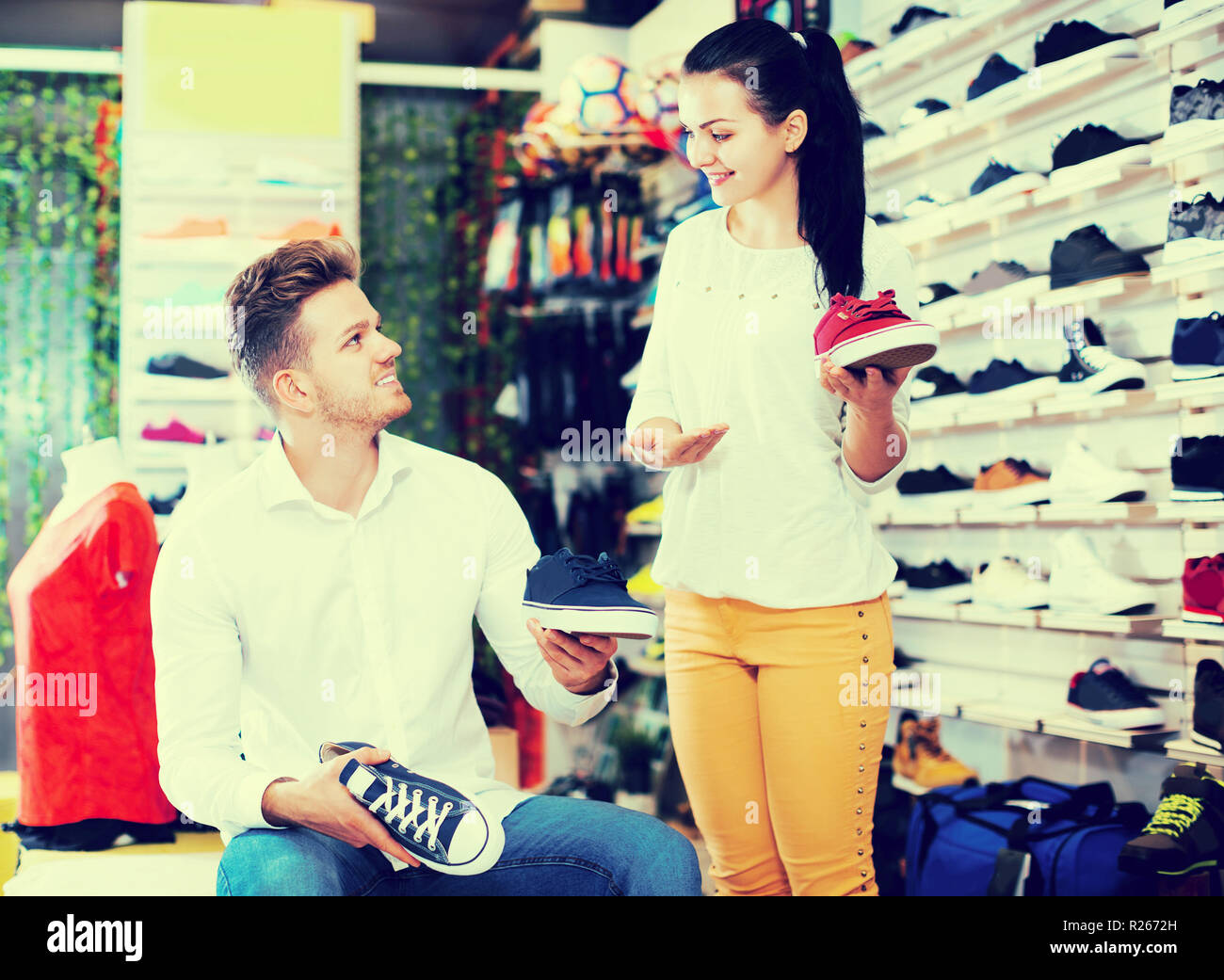 Shop assistant helping customer to choose sneakers in sports store ...