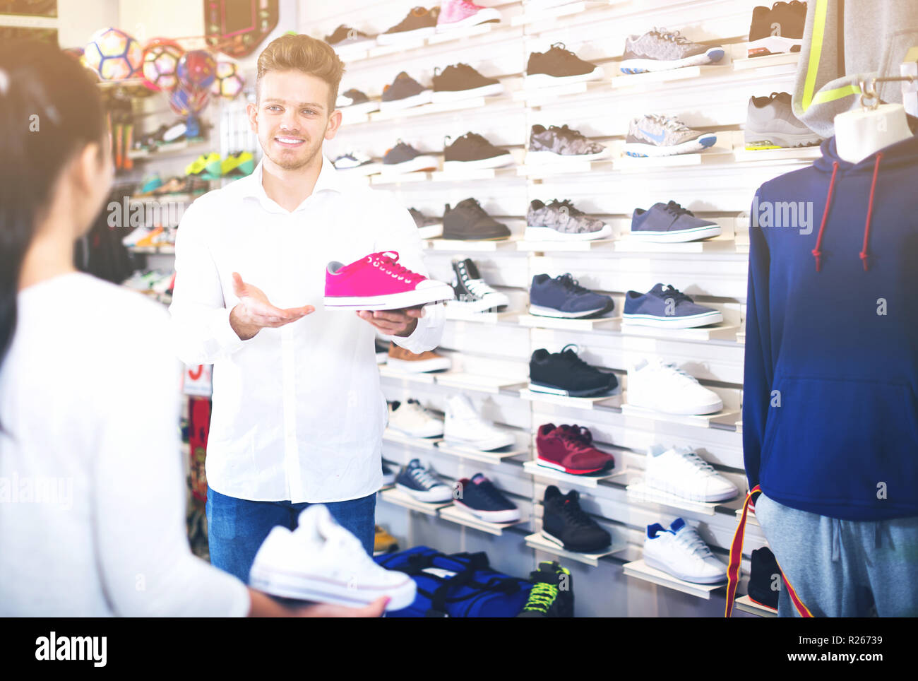 Shop assistant helping customer to choose sneakers in sports store ...