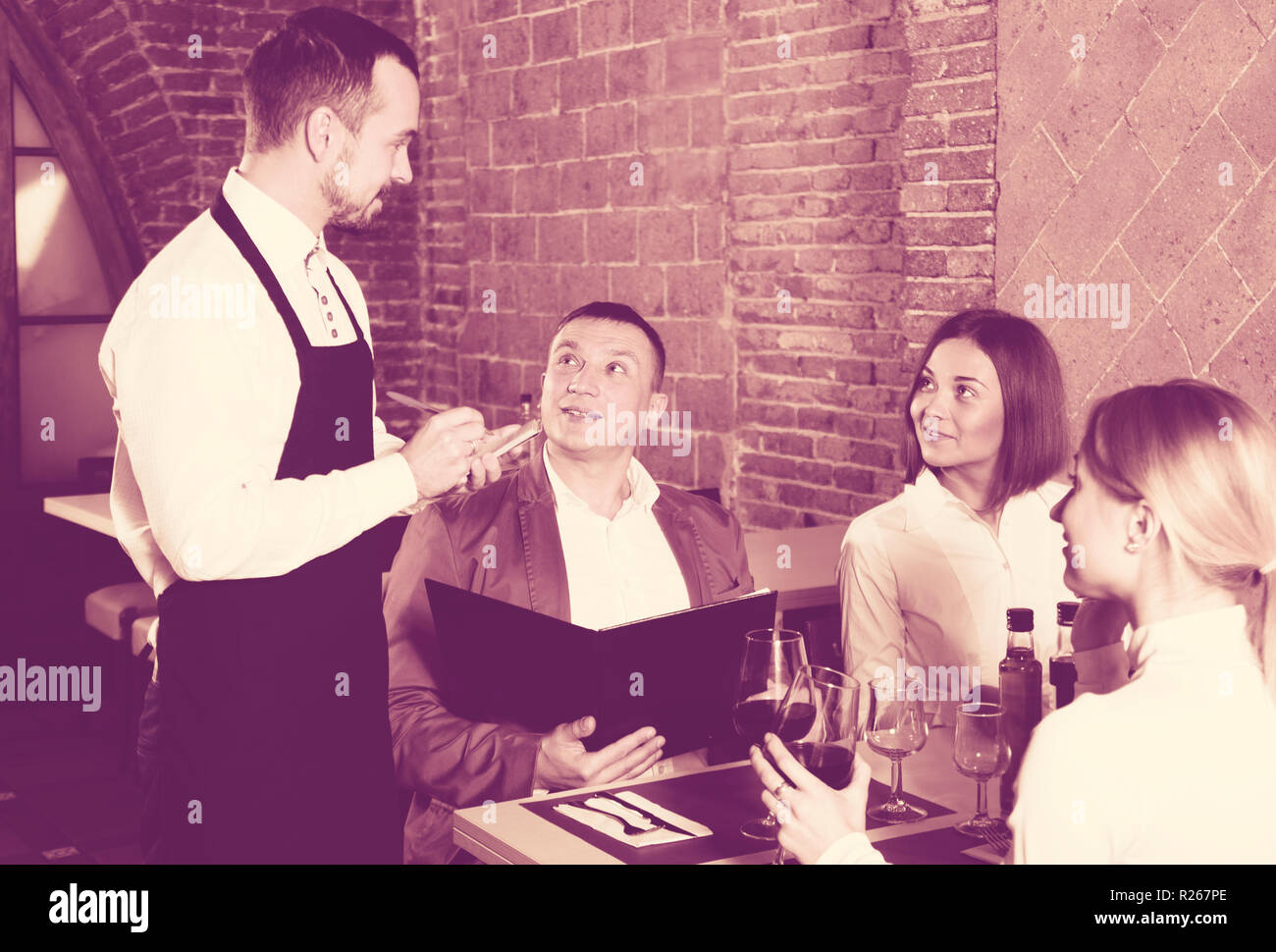 Glad male waiter writing down order from visitors in country restaurant ...