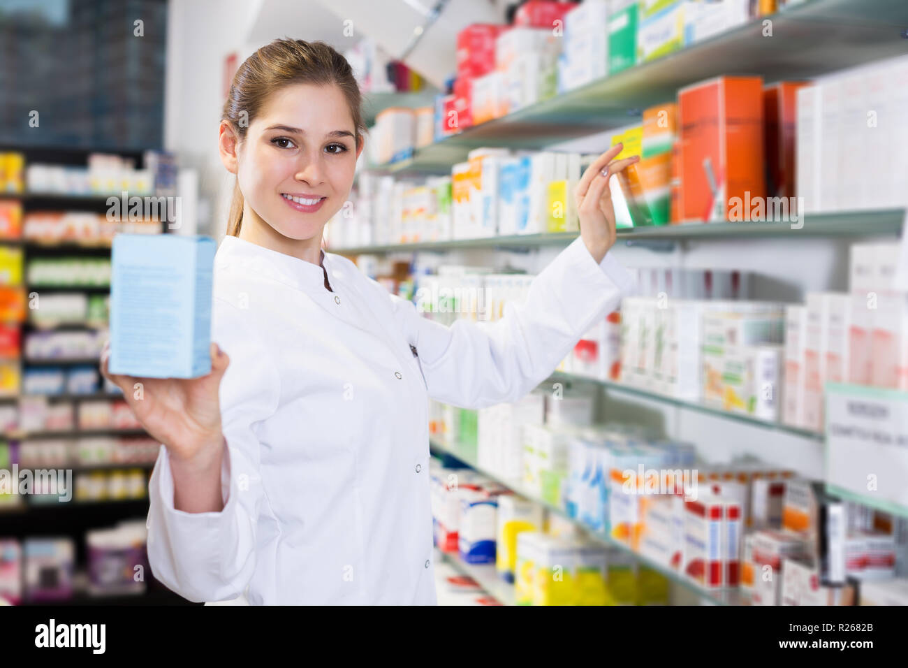 happy young pharmacist who is standing with medicine on her work place ...