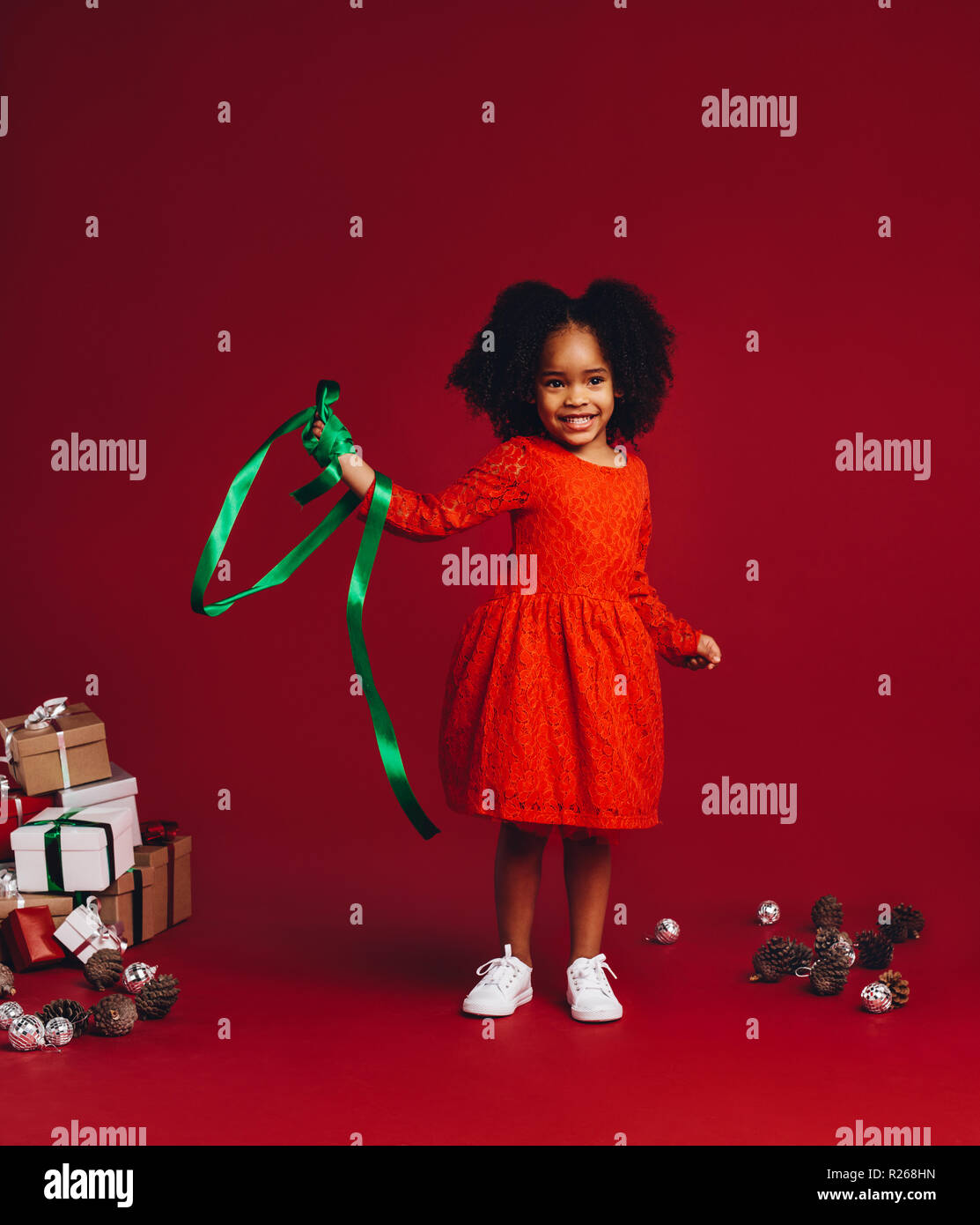 Kid playing with a decorative satin ribbon standing beside gift boxes ...