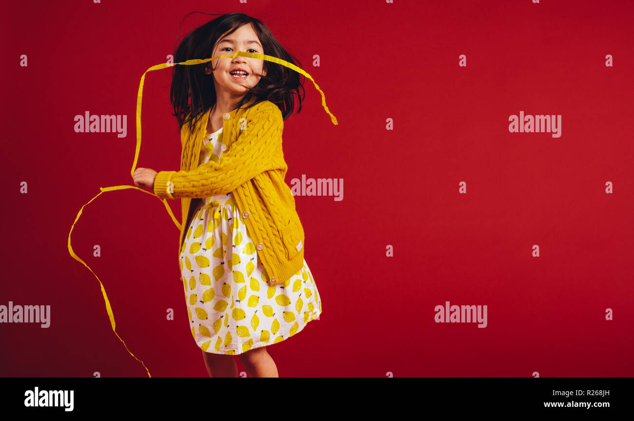Little girl playing with yellow satin ribbons. Happy asian kid waving ...