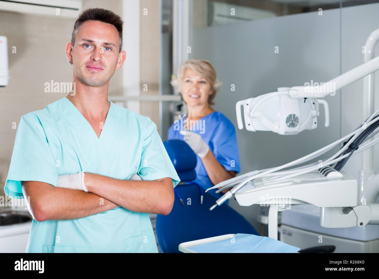Male dentist standing in dental office with hands crossed looking at ...
