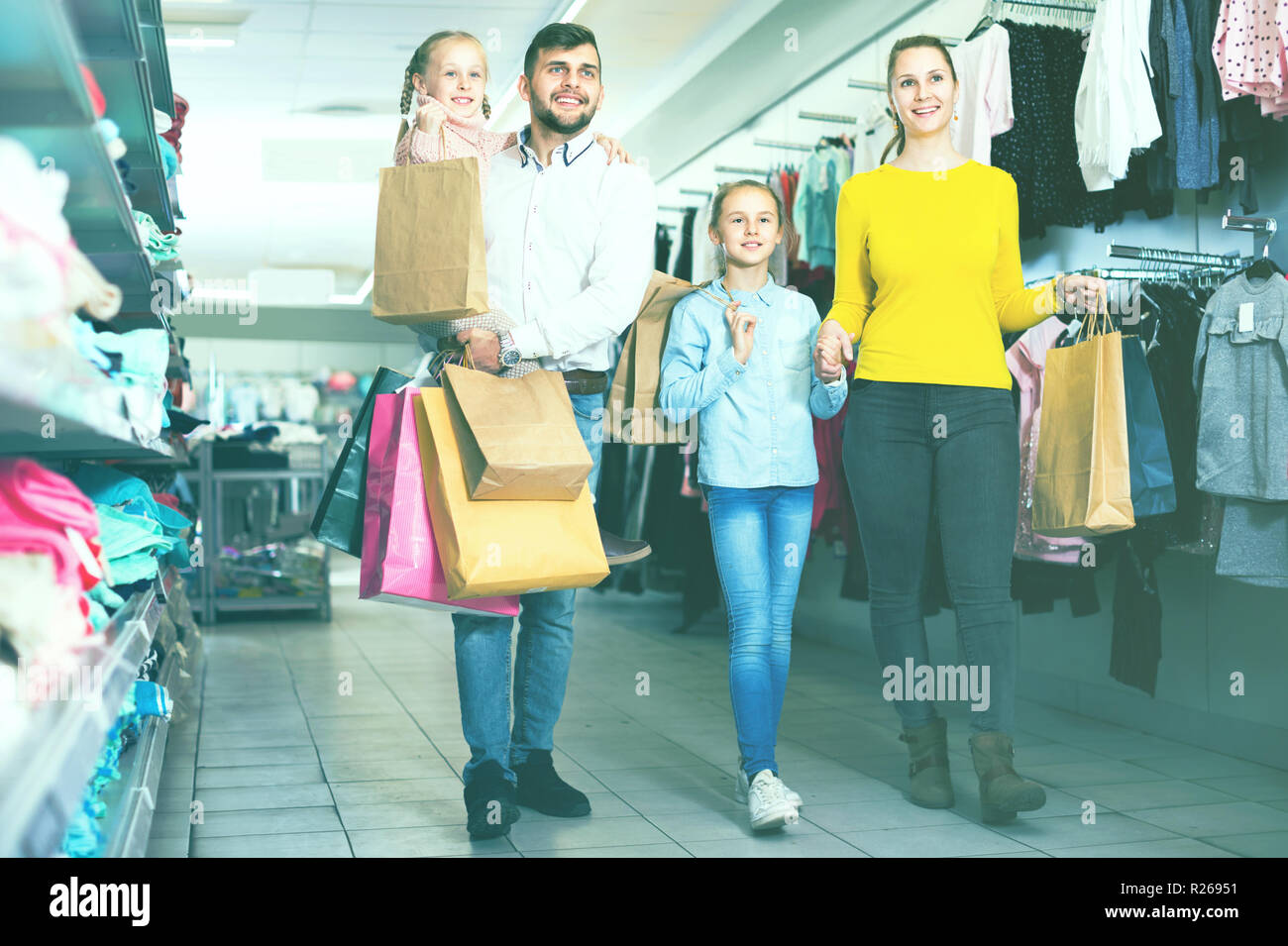 Young positive smiling parents with two little girls shopping in mall ...