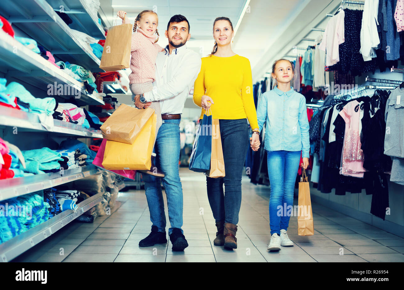 Young cheerful smiling parents with two little girls shopping in mall ...