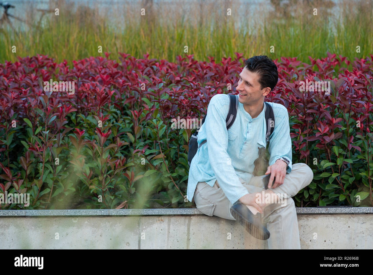 Handsome cheerful man sitting in a park and waiting Stock Photo - Alamy