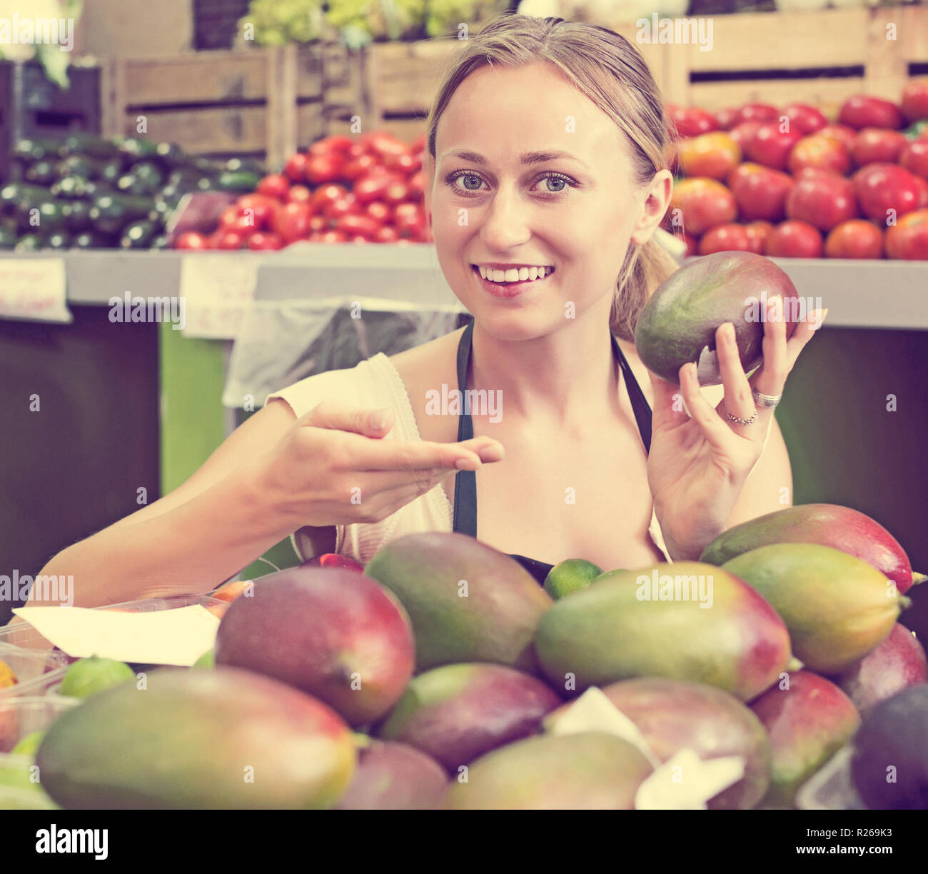 Young female seller wearing apron showing ripe mango fruits on market ...