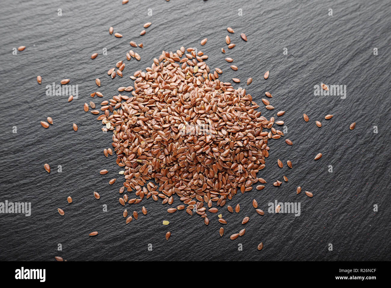 Flax seeds are scattered on a black slate background. Top view, space ...