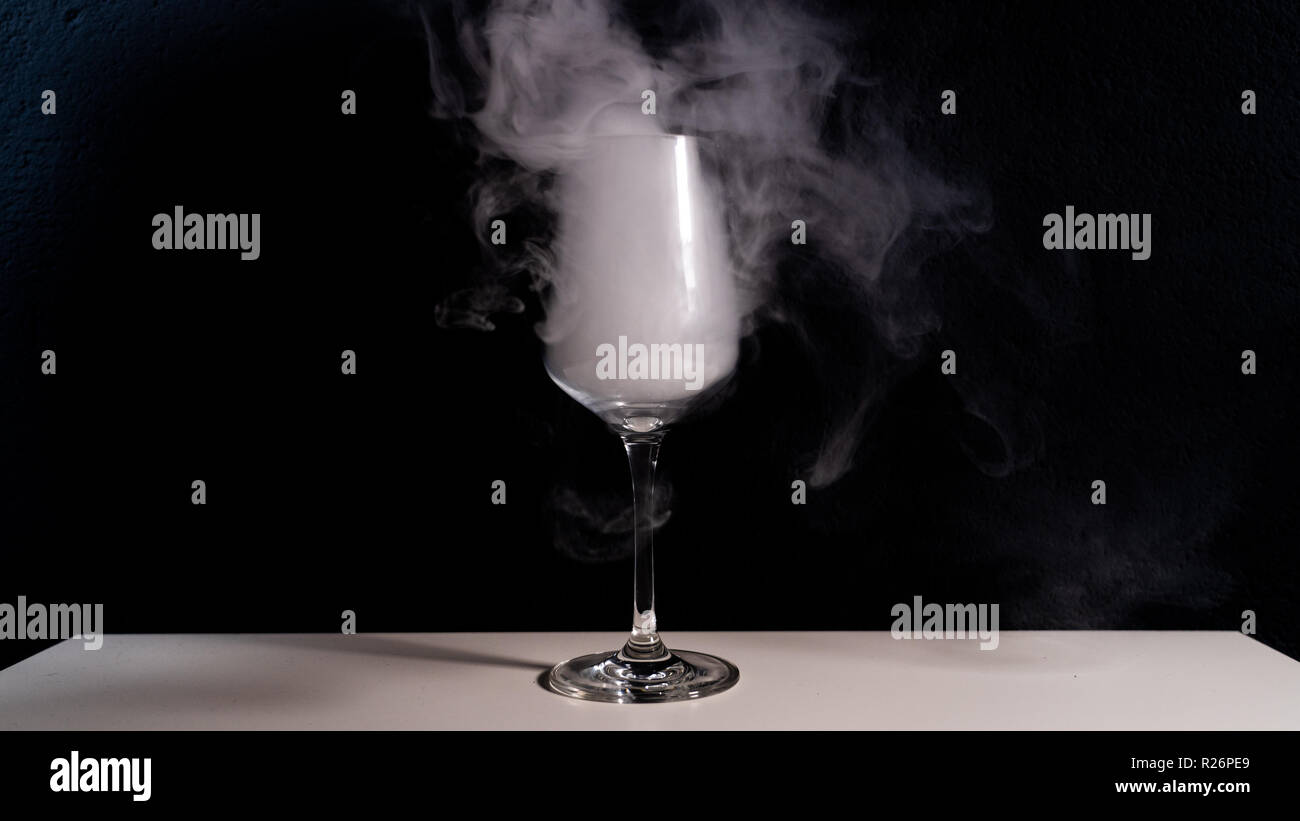 wine glas filled with smoke on a white table with a black background ...