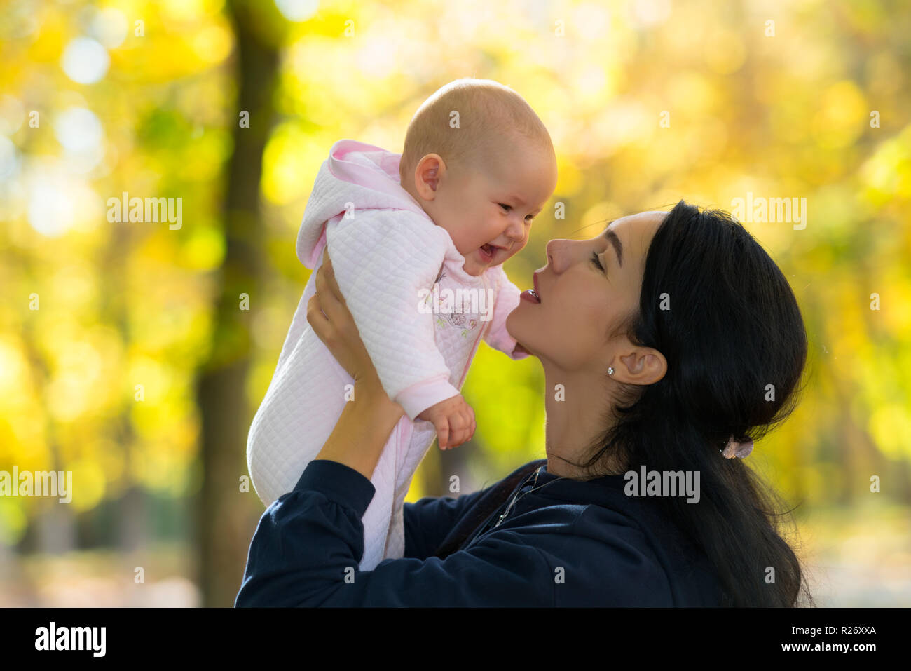 A loving mother playing with her happy, laughing baby in a park scene ...