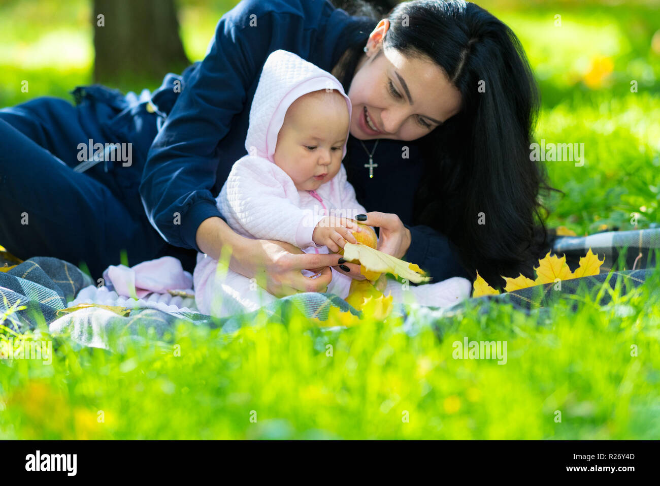 Cute little baby playing with an autumn leaf as her mother cuddles with ...